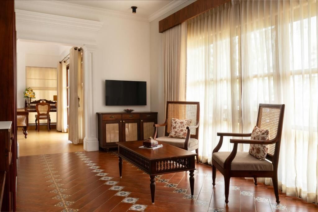 Quarto com piso de madeira, televisão, armário e duas cadeiras com almofadas.