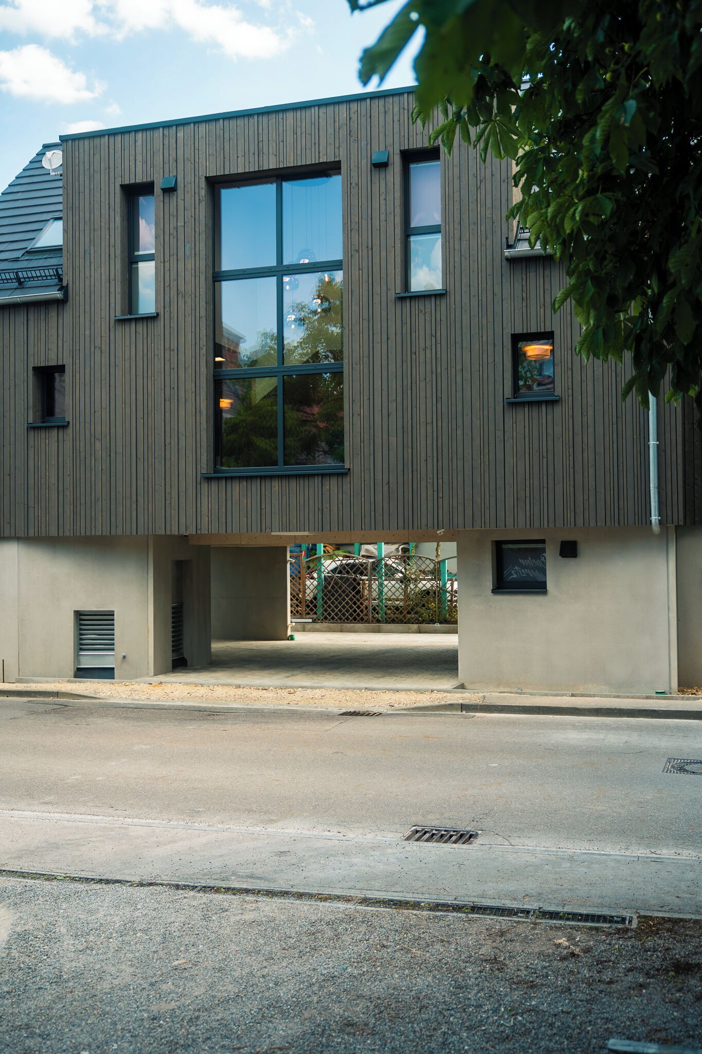 Um edifício moderno com telhado plano, janelas amplas e entrada de garagem visível.