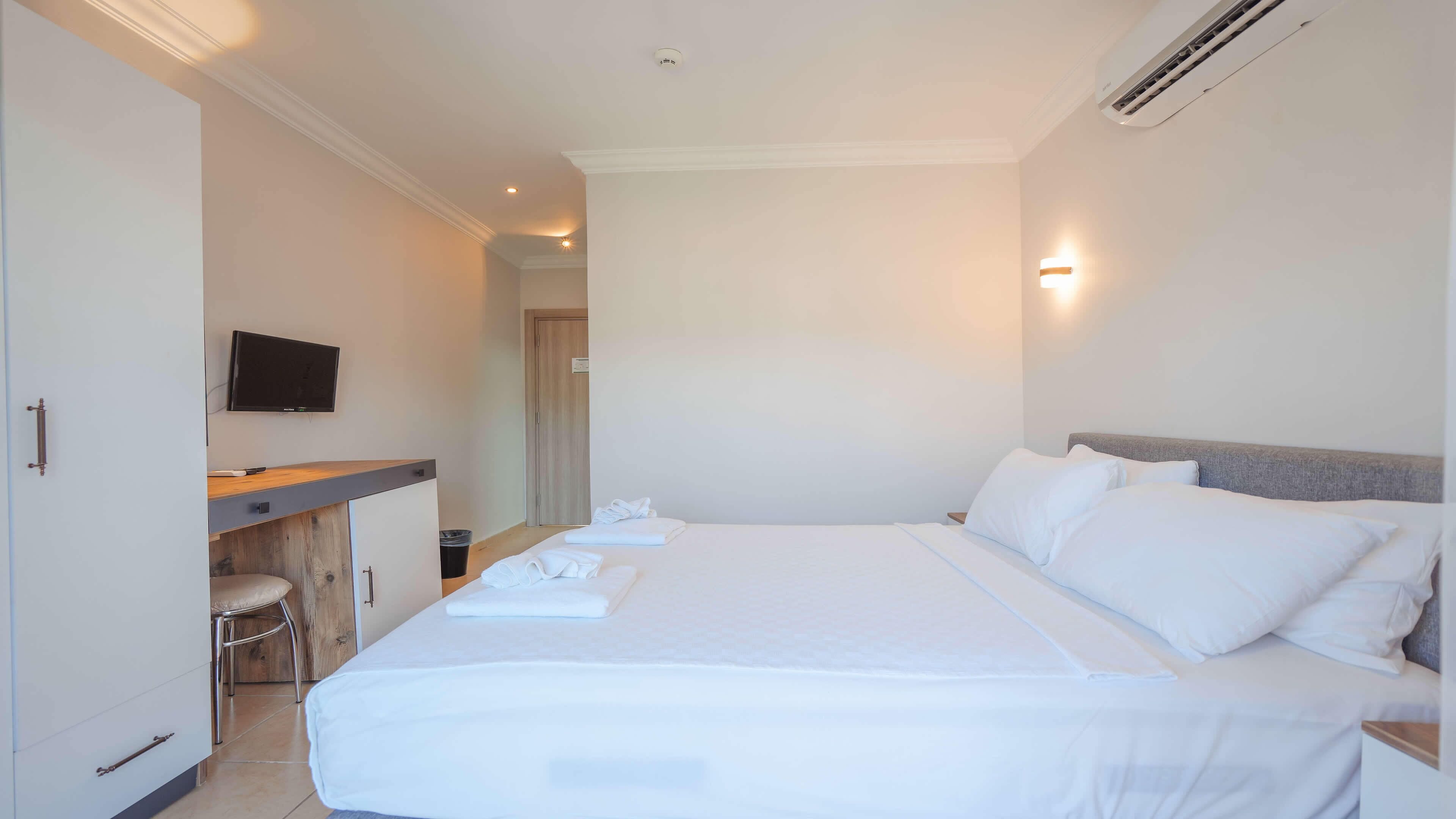 Quarto de hotel com cama, escrivaninha, cadeira, televisão e ar condicionado na parede.