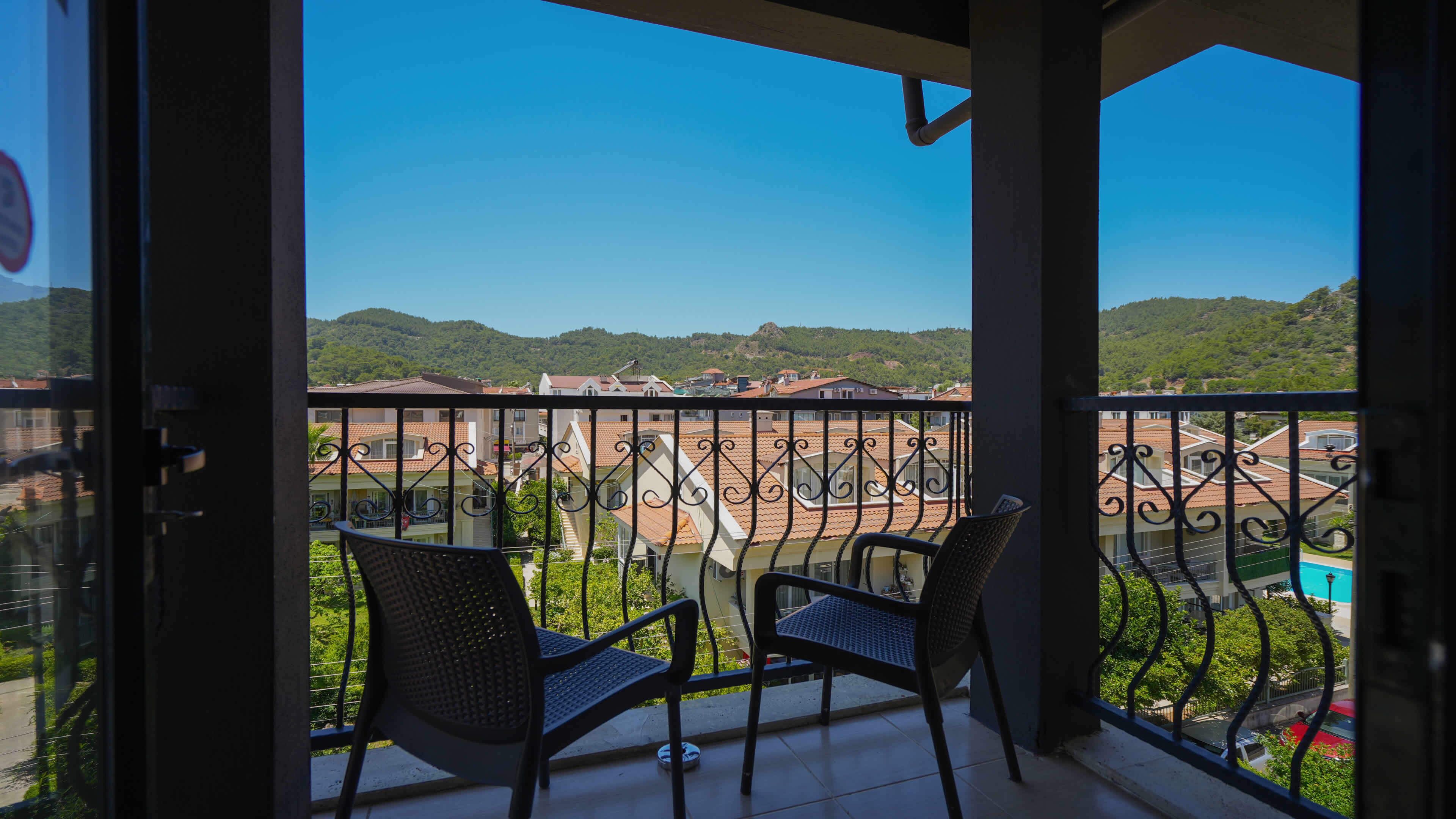Uma varanda com duas cadeiras e vista para uma área residencial, com casas e colinas.
