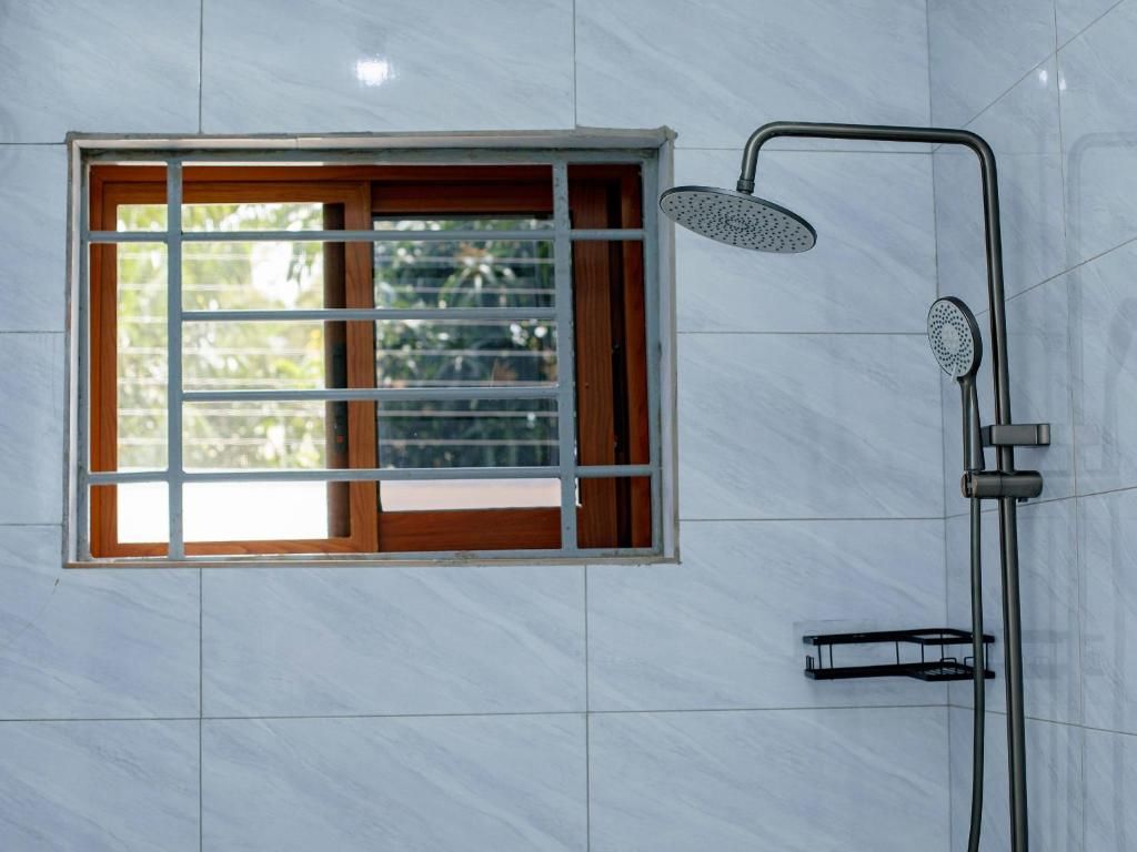 Casa de banho com chuveiro, janela com moldura de madeira e parede revestida a azulejos.