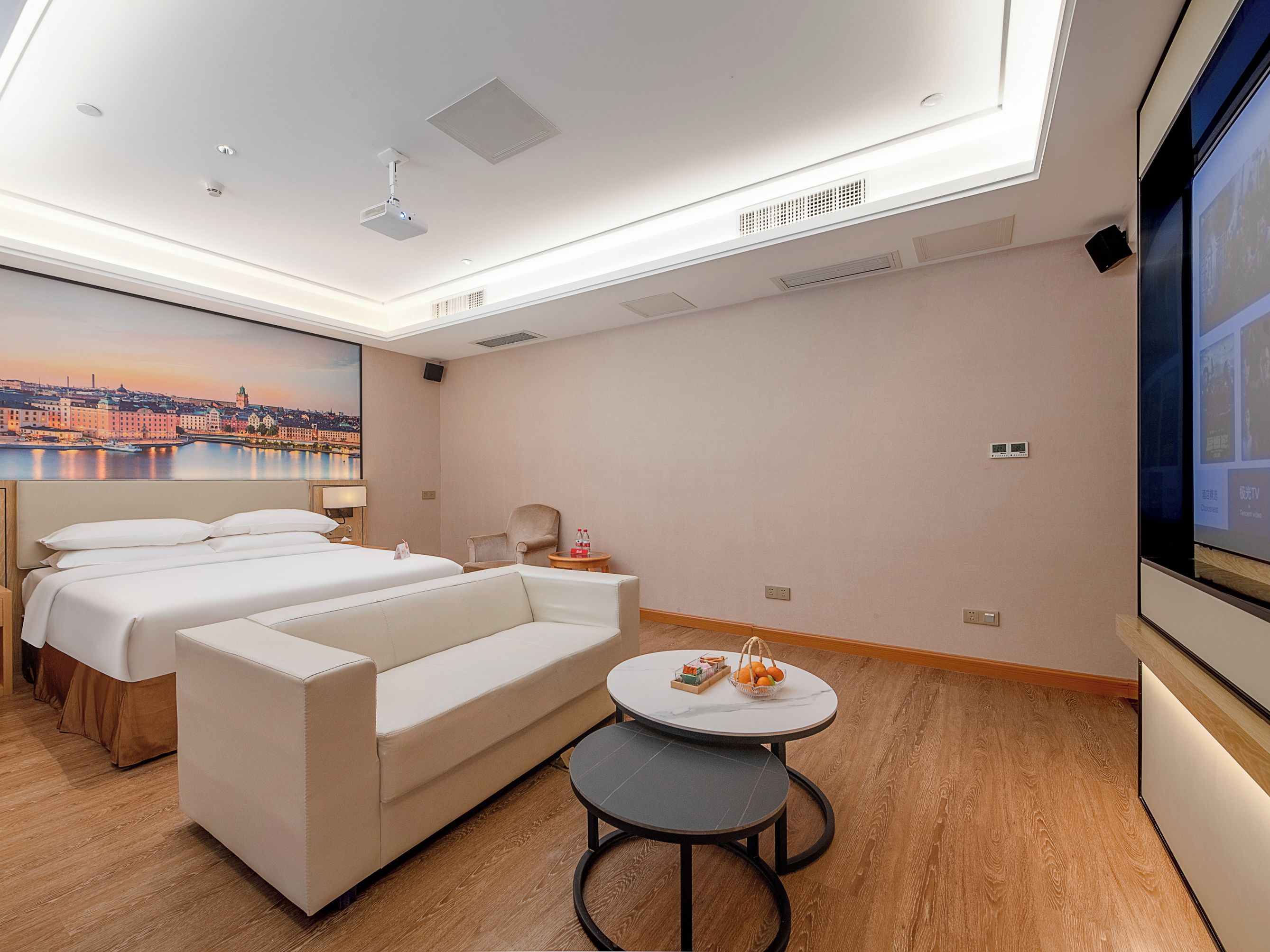 Quarto de hotel com cama, sofá, mesa pequena e tela de televisão.