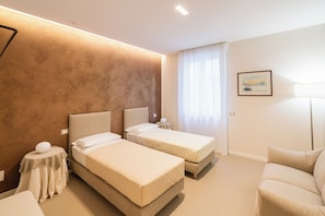 Quarto de hotel com duas camas, um sofá, uma luminária, um quadro e vista para o exterior.