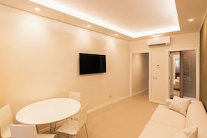 Quarto moderno com televisão de tela plana na parede, mesa redonda com cadeiras, sofá e ar condicionado.