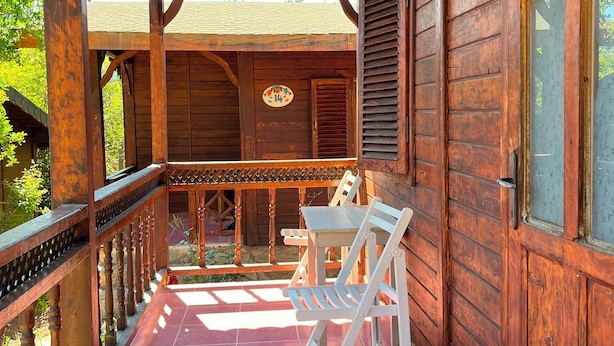 Varanda de madeira com mesa, cadeiras, corrimão e vista para um jardim.