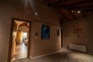 Corredor de hotel com teto de madeira, porta de acesso a um quarto e obras de arte nas paredes.