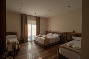Quarto de hotel com duas camas, piso de madeira e uma janela grande com cortinas.