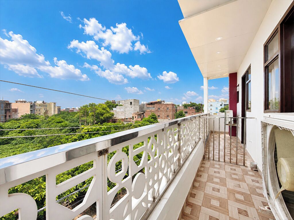Uma varanda com piso estampado, guarda-corpo branco e vista para edifícios e áreas verdes.