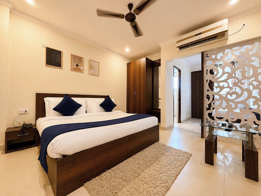 Quarto moderno com cama, mesas de cabeceira, ventilador de teto, aparelho de ar condicionado e um divisória decorativa.