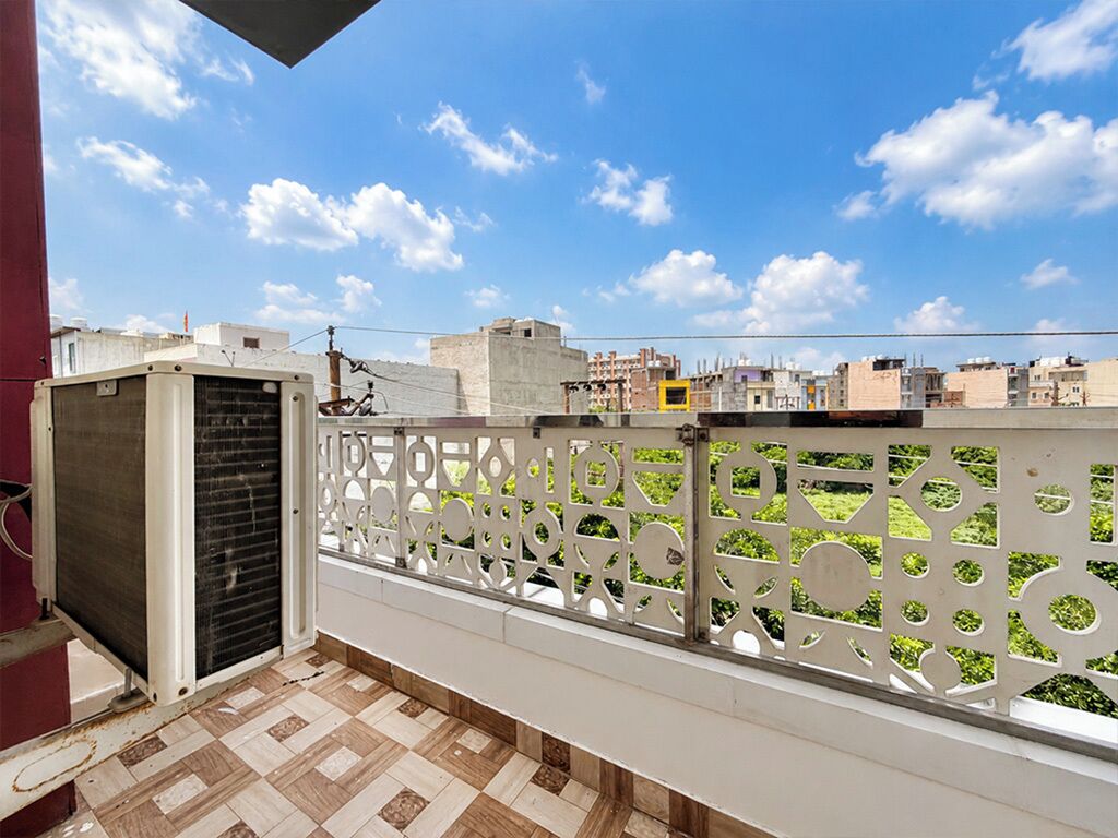 Uma varanda com piso estampado, guarda-corpo branco decorativo e vista para edifícios ao longe.