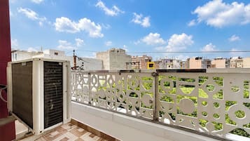 Uma varanda com piso estampado, guarda-corpo branco decorativo e vista para edifícios ao longe.