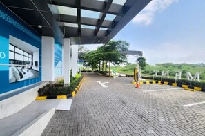 Entrada moderna de um edifício, com um caminho pavimentado que leva a uma área murada.