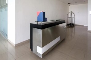 Bancada de recepção com acabamento metálico, divisória de vidro e guarda-corrimão de metal.