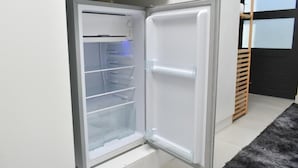 Uma geladeira moderna e vazia, com várias prateleiras, em um cômodo com uma porta preta e uma parede branca.