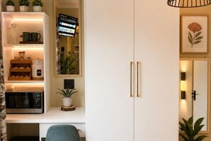 Quarto bem iluminado com um armário branco, televisão de tela plana na parede e um quadro com uma flor.
