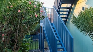 Escadaria azul que leva a um segundo andar, cercada por vegetação e um pequeno espaço de pátio com mesa e cadeiras.