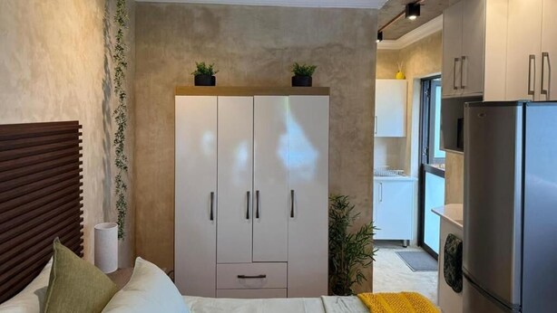 Quarto com cama, guarda-roupa e área de cozinha com frigorífico.