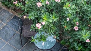 Área de pátio com mesa e duas cadeiras, rodeada por um jardim com flores cor-de-rosa.