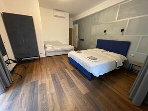 Quarto de hotel com cama, uma cadeira, guarda-roupa e porta.