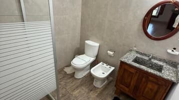 Casa de banho com chuveiro, sanita, bidé e toucador com espelho.