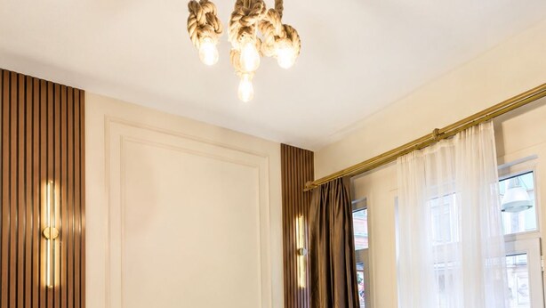 Quarto de hotel com uma cama grande, mesas de cabeceira, um candelabro, cortinas e vista para o exterior.