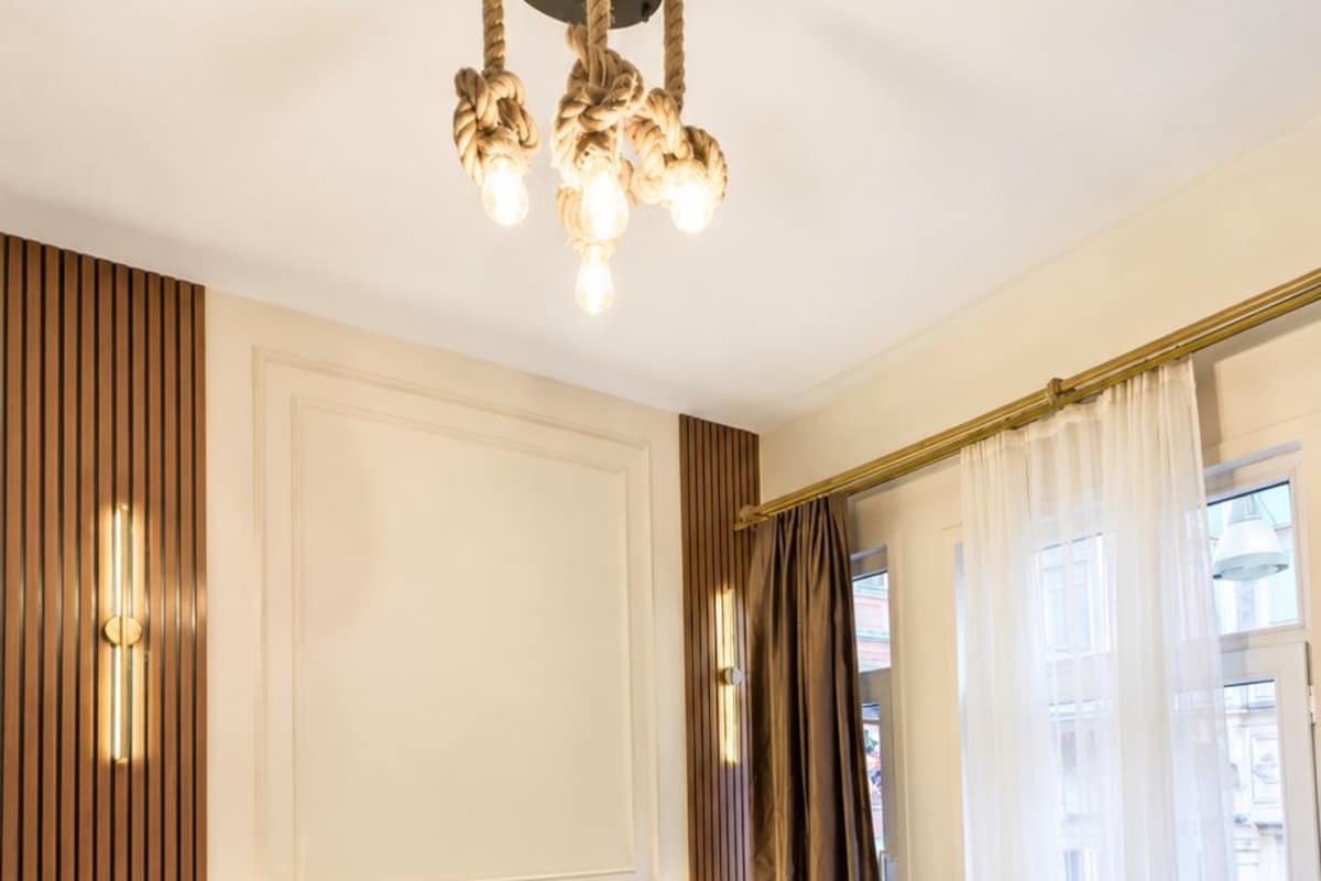 Quarto de hotel com uma cama grande, mesas de cabeceira, um candelabro, cortinas e vista para o exterior.
