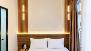 Quarto de hotel com cama, mesas de cabeceira, luminária na parede e janela com cortinas.