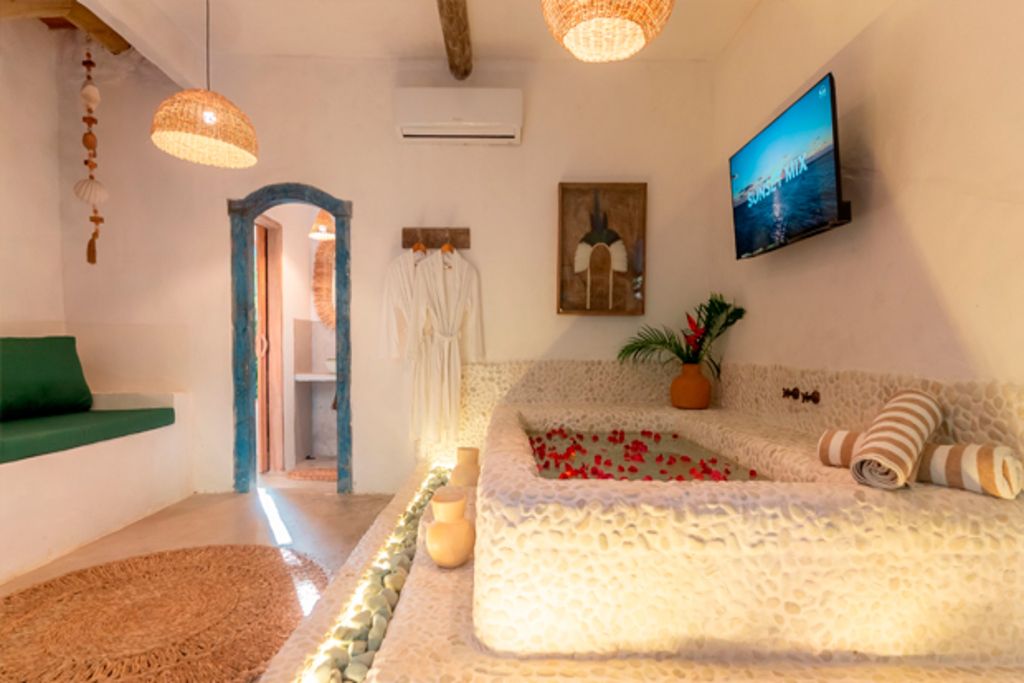 Um quarto de spa com banheira de pedra, televisão e um quadro na parede.