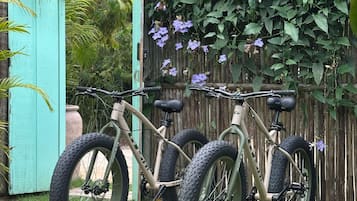 Duas bicicletas estacionadas em um jardim com cerca de madeira e vegetação ao fundo.