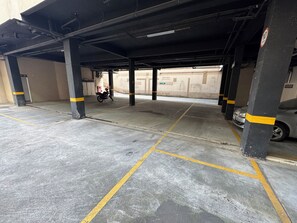 Uma garagem de estacionamento com pisos de concreto, linhas amarelas e pilares pretos com listras amarelas.