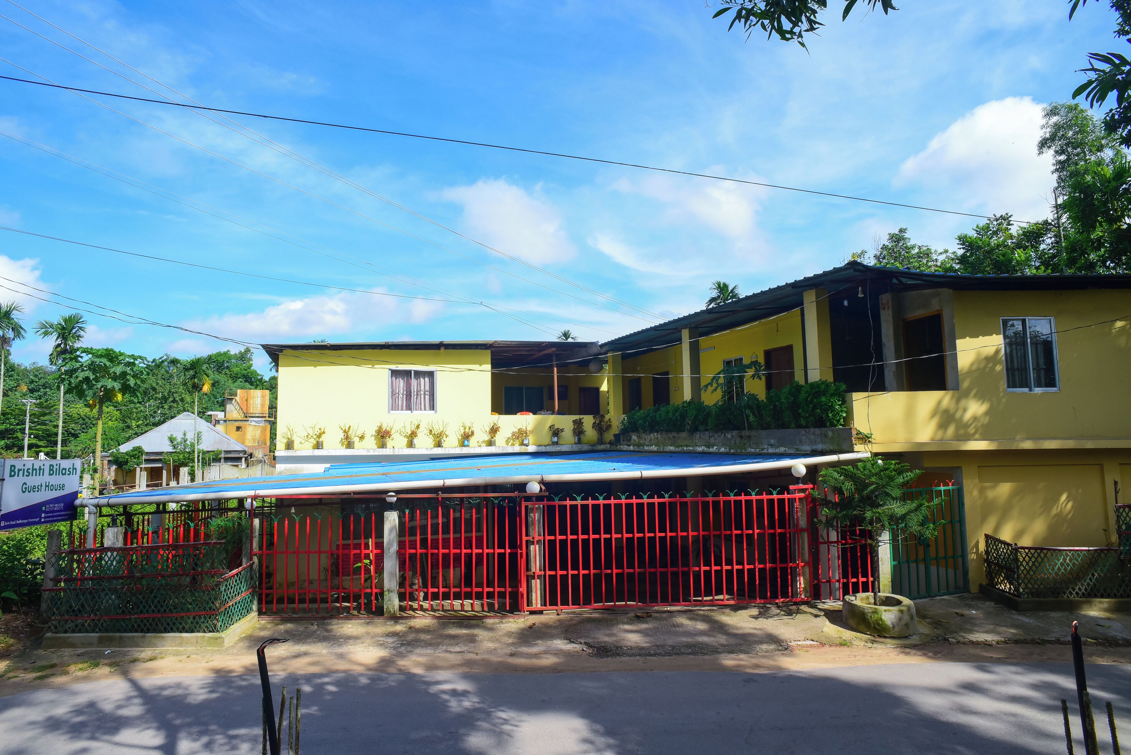 Um edifício de dois andares com fachada amarela, portão vermelho e toldo azul.