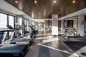 Academia moderna com equipamentos de cardio, estações de musculação e espelho grande.