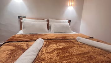 Quarto de hotel com uma cama, duas luminárias fixadas na parede e teto de madeira.