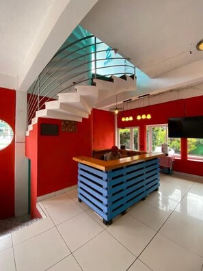 Um interior moderno com uma recepção central, uma escadaria curva e uma grande janela que traz luz natural.