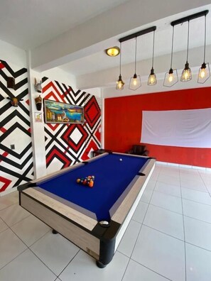 Uma mesa de bilhar com pano azul, rodeada por um chão de azulejos brancos.