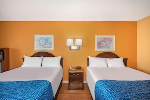 Quarto de hotel com duas camas, uma mesa de cabeceira com abajur e dois quadros florais emoldurados na parede.