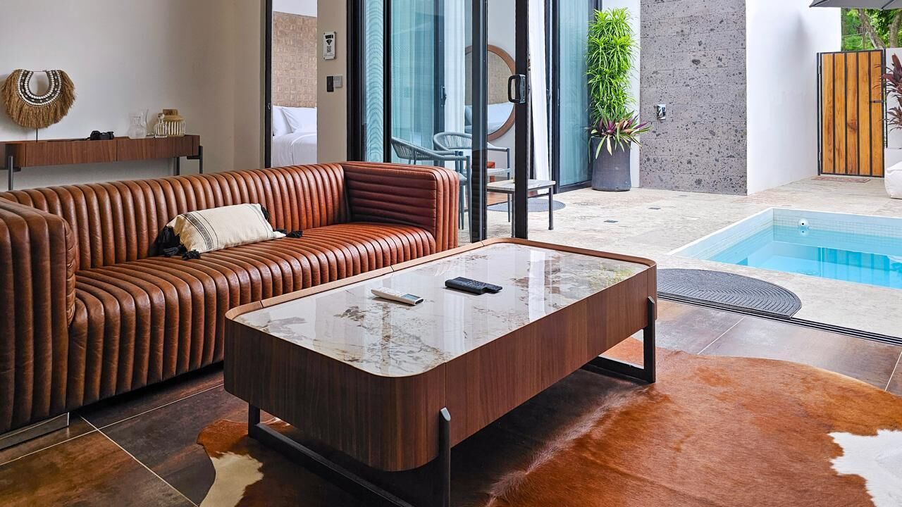 Uma sala de estar moderna com sofá de couro, mesa de centro de vidro e vista para a piscina.