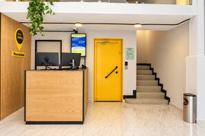 Balcão de recepção de hotel com acabamento em madeira, uma tela digital e um aviso com tarifas de quartos.