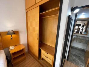 Quarto com guarda-roupa de madeira, mesa de cabeceira com abajur e espelho.