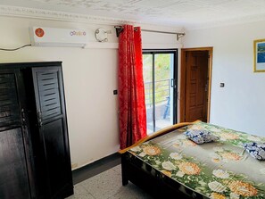 Quarto com cama, guarda-roupa, janela com cortinas vermelhas e porta.