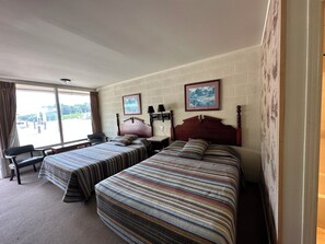 Quarto de hotel com duas camas, uma escrivaninha, uma cadeira e uma janela com cortinas.