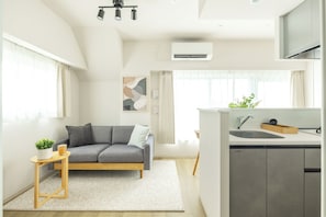 Uma sala de estar moderna com um sofá cinza, uma pequena mesa de madeira e um tapete branco.