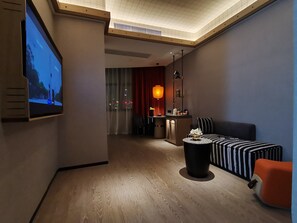 Uma sala de estar moderna com televisão de tela plana, um sofá, uma mesa de centro e um espaço de jantar com cortina vermelha.