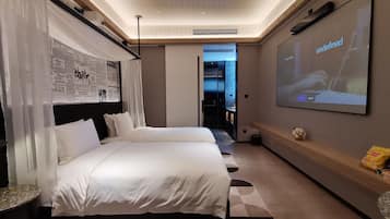 Quarto de hotel com duas camas, uma tela grande exibindo 'undefined' e uma parede com recortes de jornais.