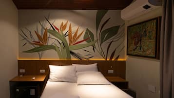 Quarto de hotel com cama, duas mesas de cabeceira, ar condicionado fixado na parede e um quadro.