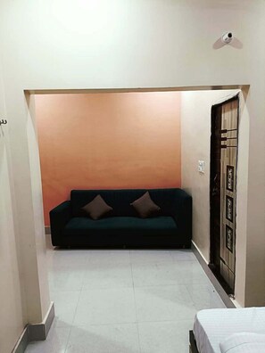 Quarto pequeno com sofá verde escuro em parede cor de pêssego, uma cama branca e uma porta com detalhe decorativo.