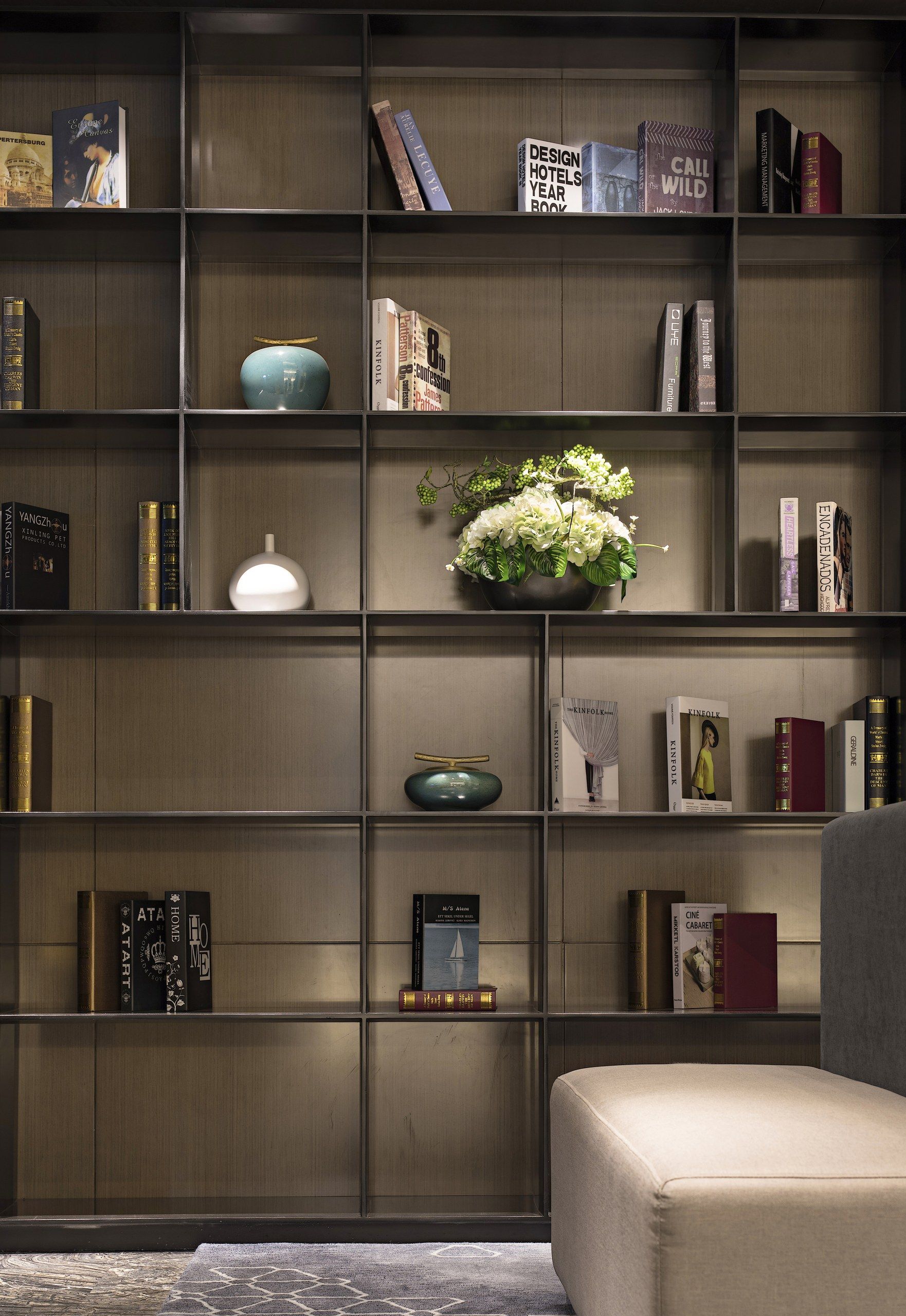 Uma estante com diversos livros, objetos decorativos e um vaso com flores.