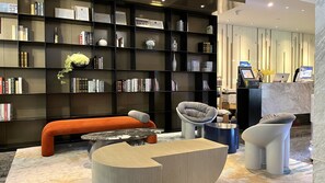 Um lobby moderno com uma grande estante de livros, um balcão de recepção e assentos contemporâneos.