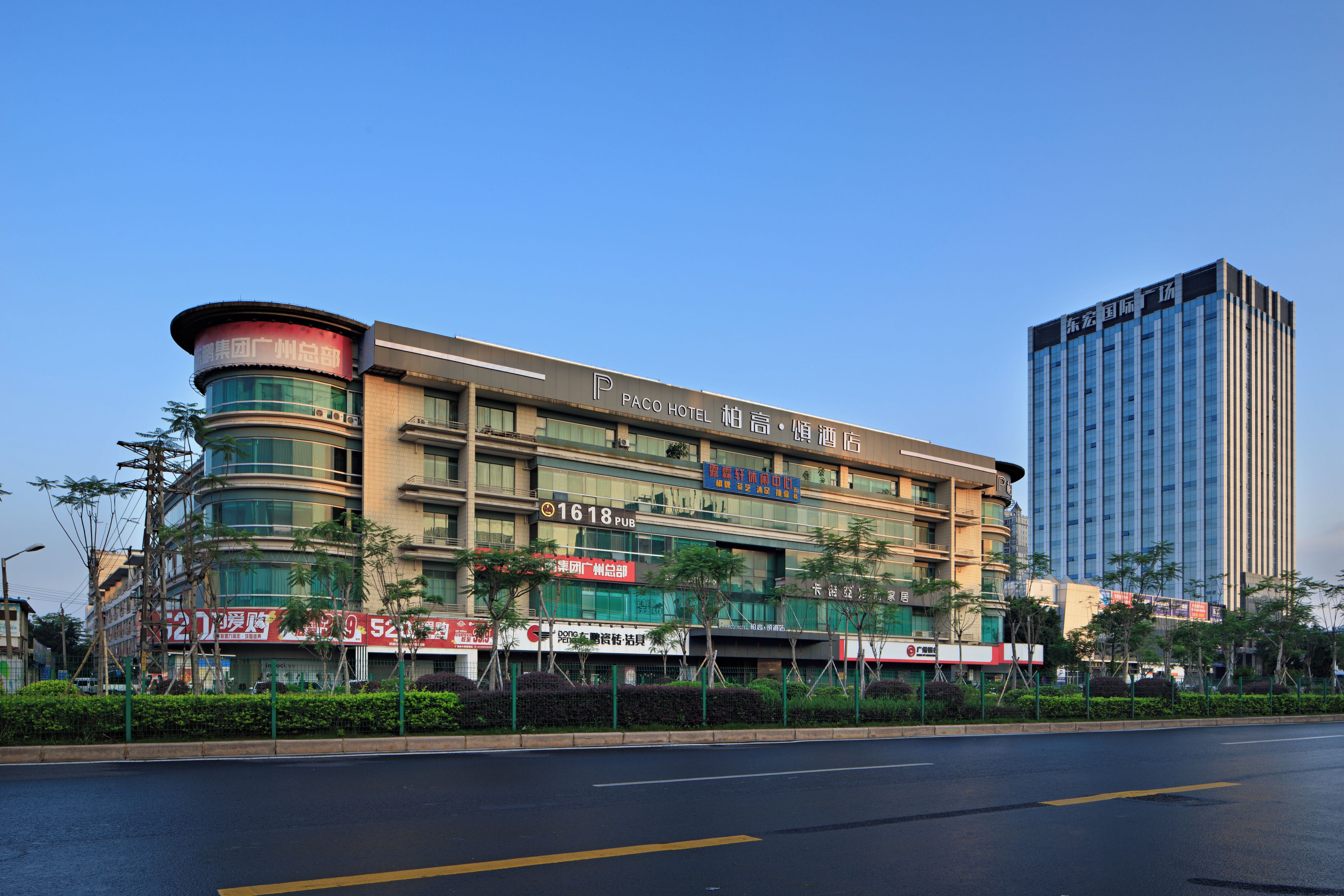 Um hotel com vários andares, com uma placa de destaque 'Paco Hotel', um '1618 Pub' no andar térreo e um edifício alto adjacente.