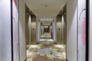 Corredor longo e estreito de hotel, com portas em ambos os lados, carpete estampado e teto com iluminação embutida.